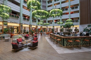 Um amplo átrio com vários níveis, apresentando um bar central com banquetas, áreas de estar e jardins verticais exuberantes.