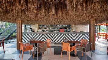 Uma área de bar ao ar livre com um telhado de palha, parede com padrão herringbone e diversas opções de assentos.