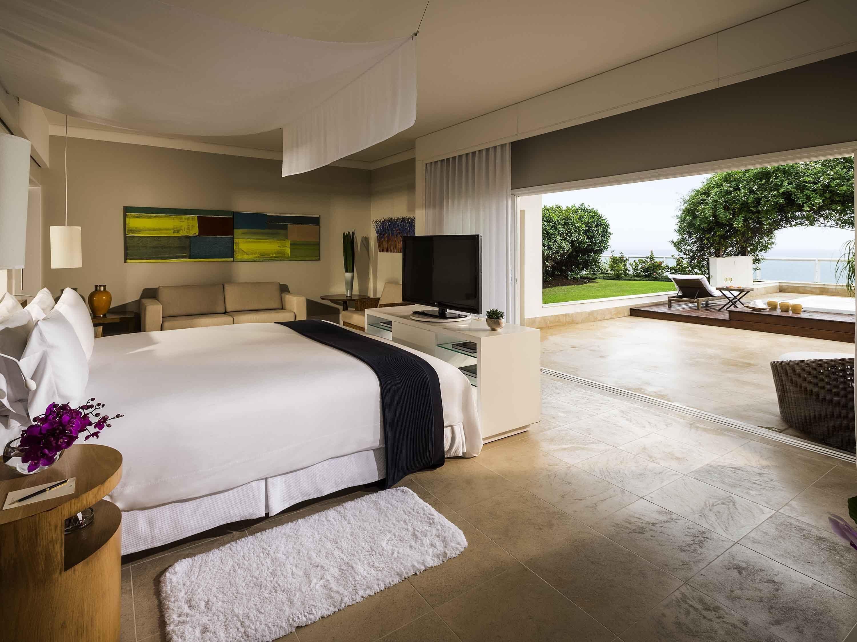 Quarto de hotel moderno com uma cama grande, televisão de tela plana, escrivaninha e varanda com vista para o mar.