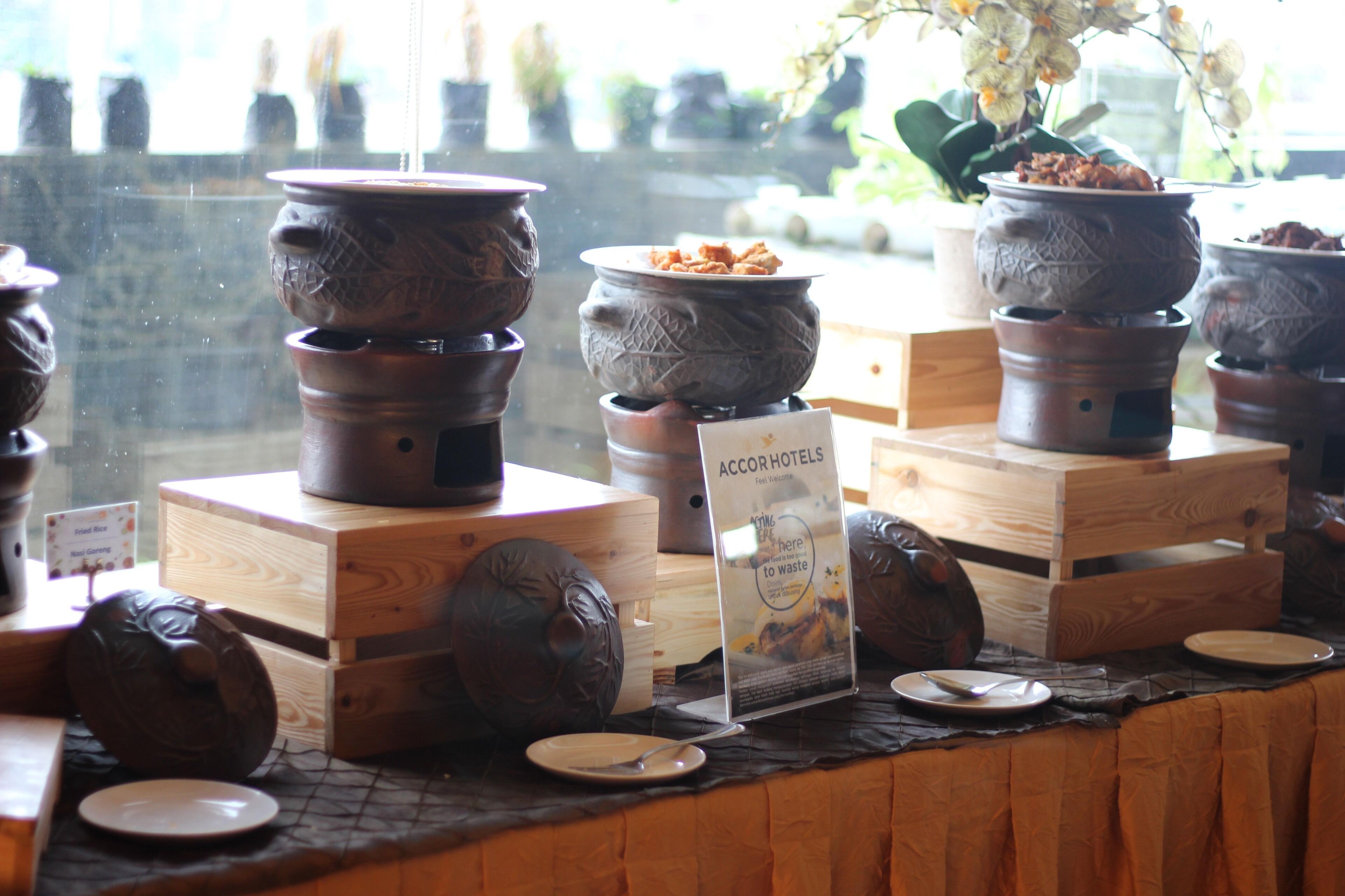 Exposição de potes de barro tradicionais com comida, dispostos em suportes de madeira em um quarto com vista para a janela.