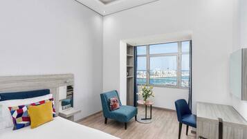 Quarto de hotel moderno com uma cama grande, escrivaninha, cadeira e janela com vista para a cidade.