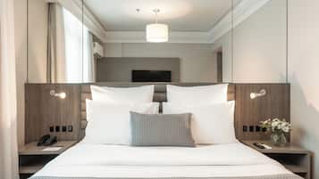 Quarto de hotel com uma cama grande, mesa de cabeceira com telefone, vaso com flores e televisão fixada na parede.