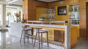 Uma área de bar com bancadas de granito, banquetas de madeira e uma tela de televisão.