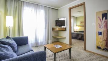 Quarto de hotel com sofá, uma mesinha, televisão, quadro e espelho.