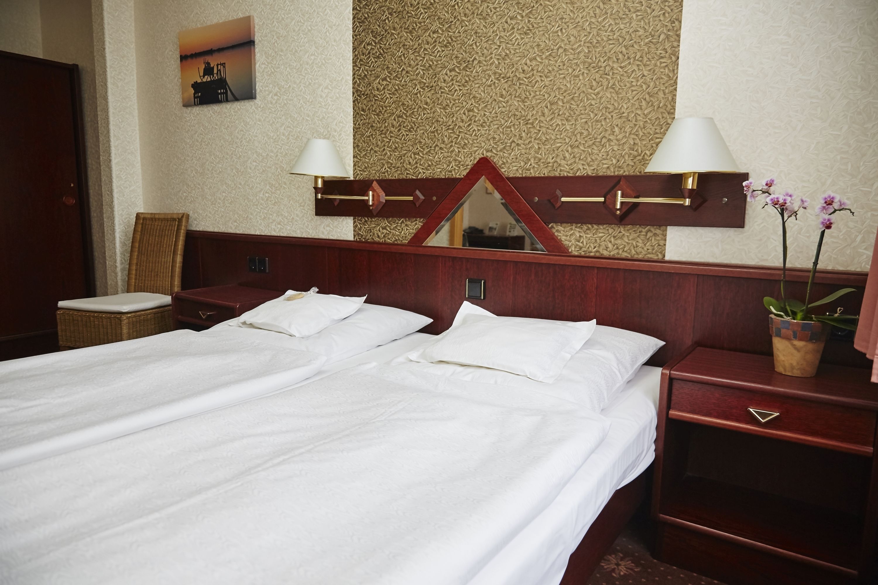 Quarto de hotel com uma cama grande, duas mesas de cabeceira, um espelho e uma luminária na parede.
