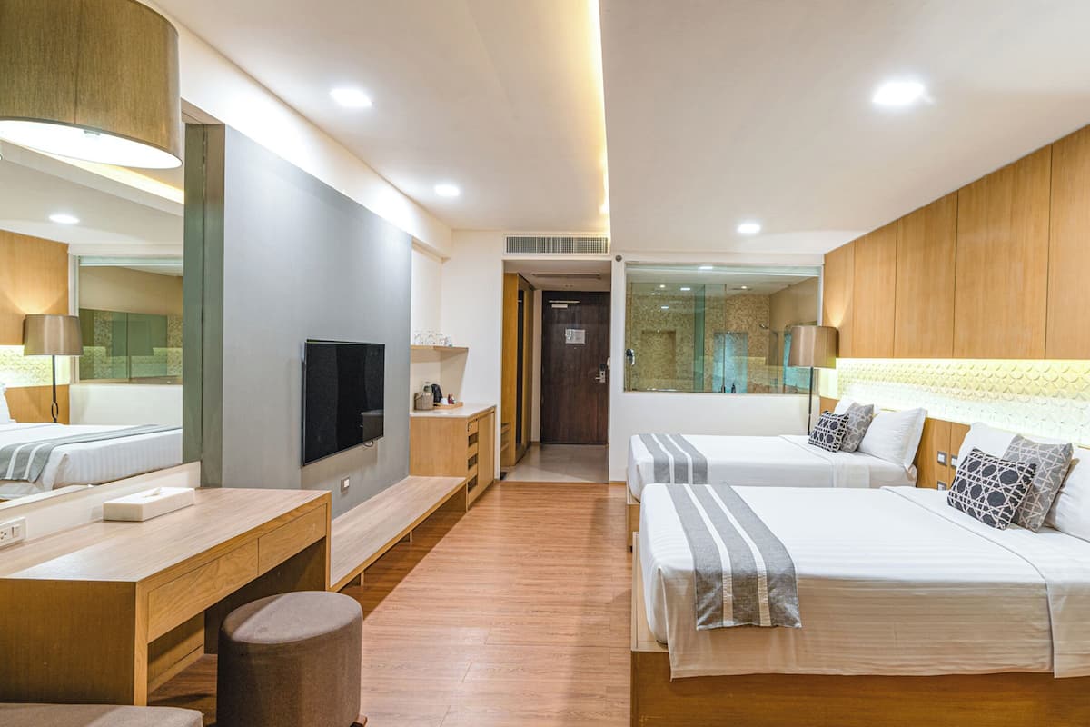 Quarto de hotel com duas camas, uma escrivaninha, televisão e casa de banho visível através de um separador de vidro.