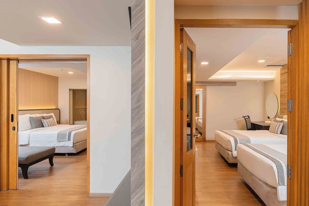 Quarto de hotel moderno com piso de madeira, duas camas, uma escrivaninha e um espelho.