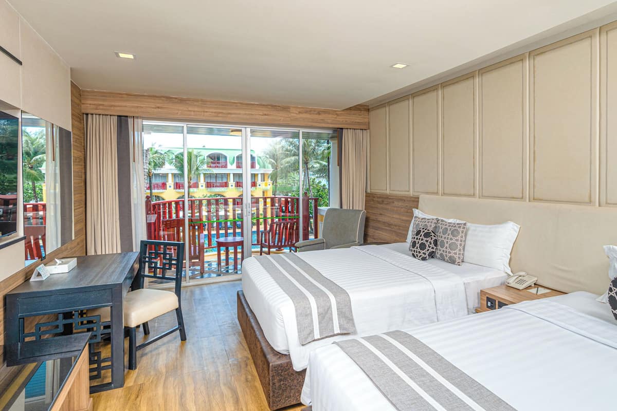 Quarto de hotel com duas camas, uma escrivaninha e vista para uma piscina e um edifício.