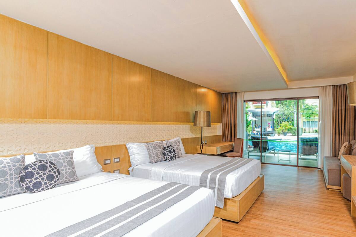 Quarto de hotel com duas camas, uma escrivaninha, uma cadeira e vista para a área da piscina.