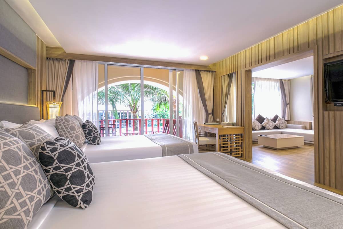 Quarto de hotel com cama, sofá, televisão e varanda com vista para palmeiras.