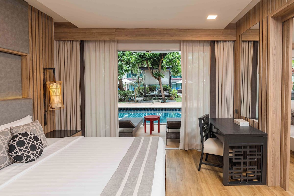 Quarto de hotel com cama, escrivaninha, sofá e vista para uma piscina ao ar livre.