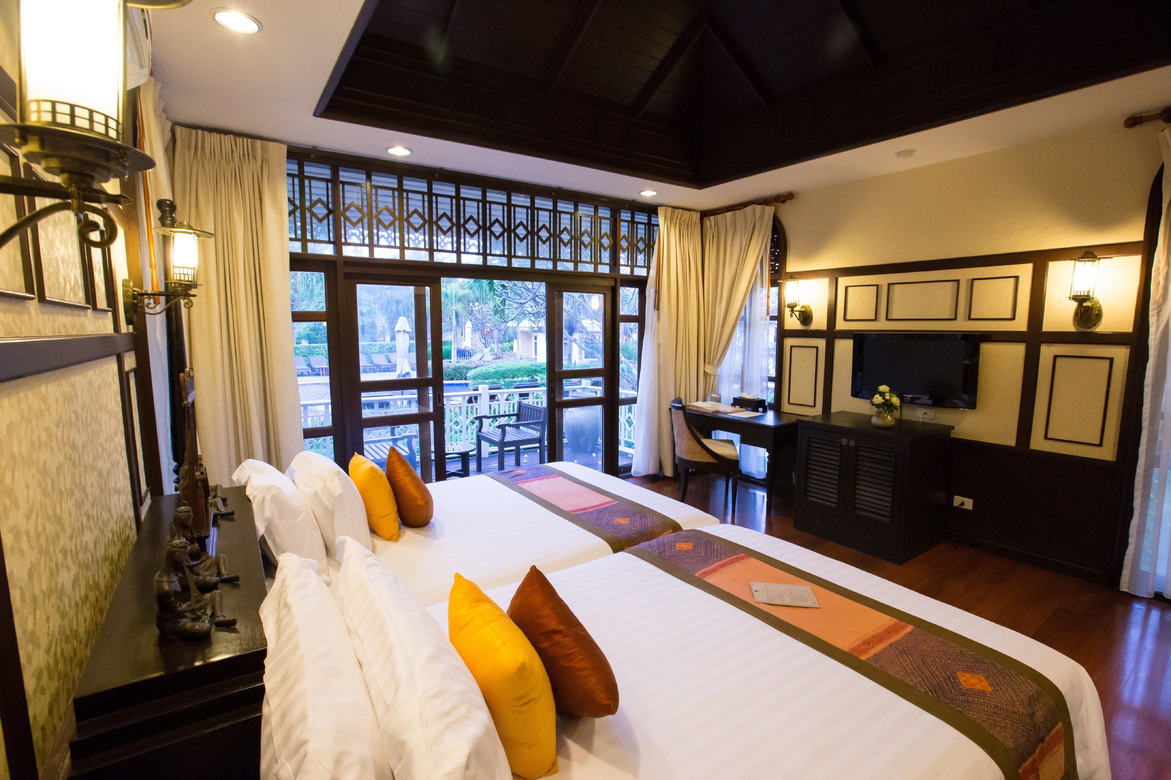 Quarto de hotel com duas camas, uma escrivaninha, televisão e vista para a varanda.