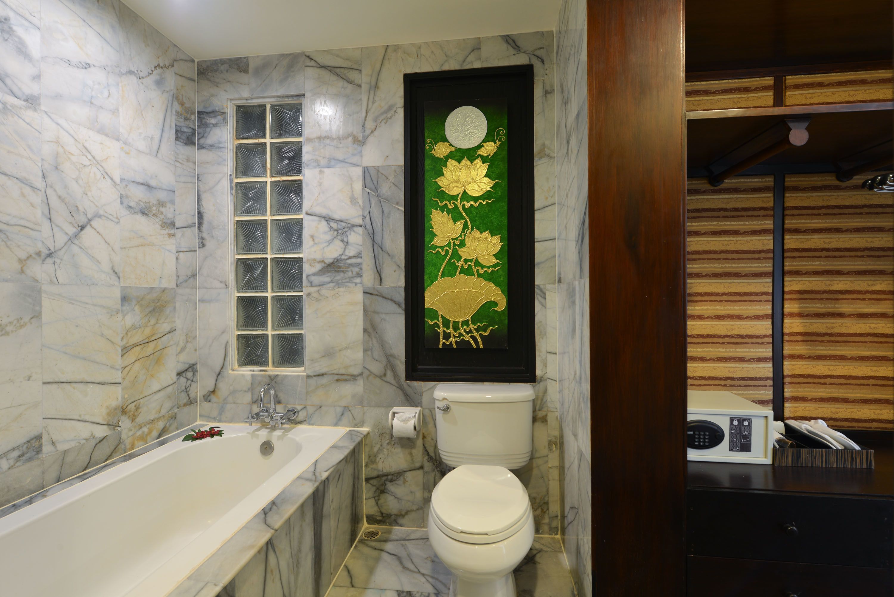 Uma casa de banho com parede de mármore, banheira, sanita e uma obra de arte emoldurada sobre a sanita.
