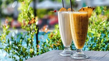 Duas altas taças com bebidas, canudos e um enfeite, sobre uma mesa com um fundo desfocado ao ar livre.