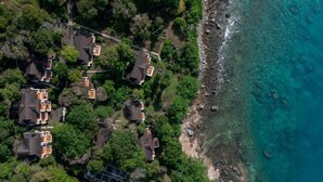 Vista aérea de uma área residencial costeira com casas rodeadas por vegetação densa e um mar azul límpido.