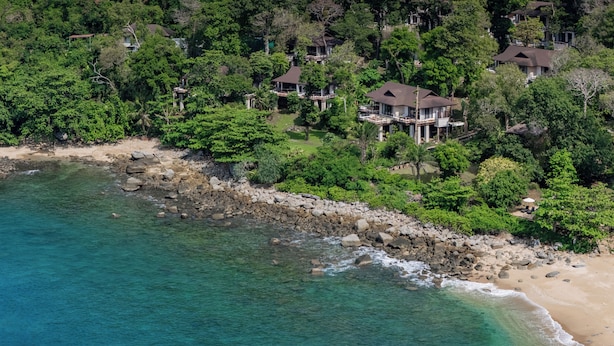 Vista aérea de uma propriedade costeira com várias casas, rodeadas por vegetação densa e uma linha costeira rochosa.