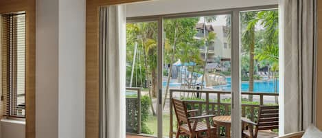 Quarto de hotel com uma grande porta de correr de vidro que dá para uma área de piscina, móveis de madeira e vista para a piscina e vegetação ao redor.
