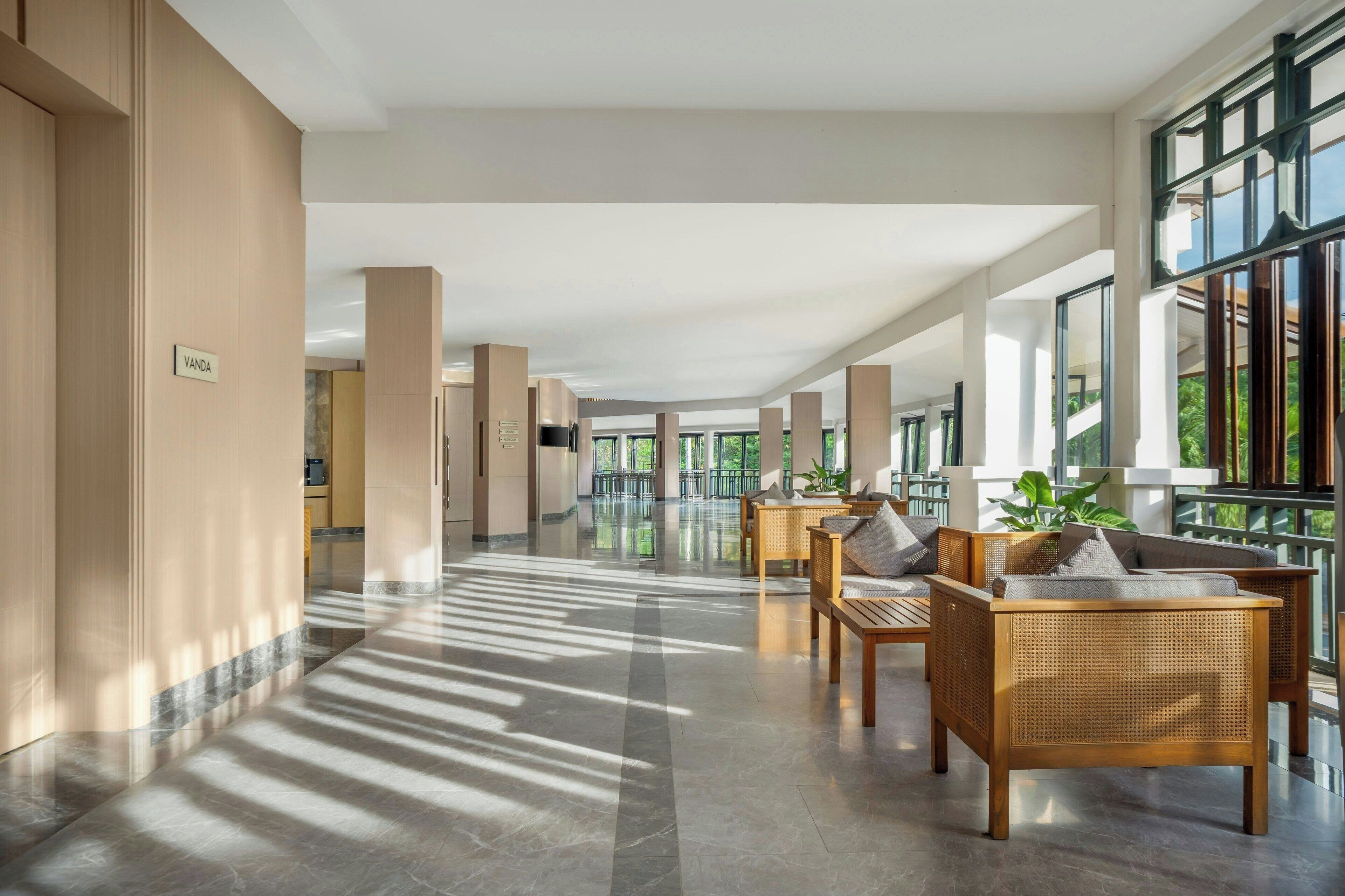 Um amplo saguão de hotel com design moderno, apresentando um corredor longo, áreas de estar confortáveis e grandes janelas que proporcionam iluminação natural.