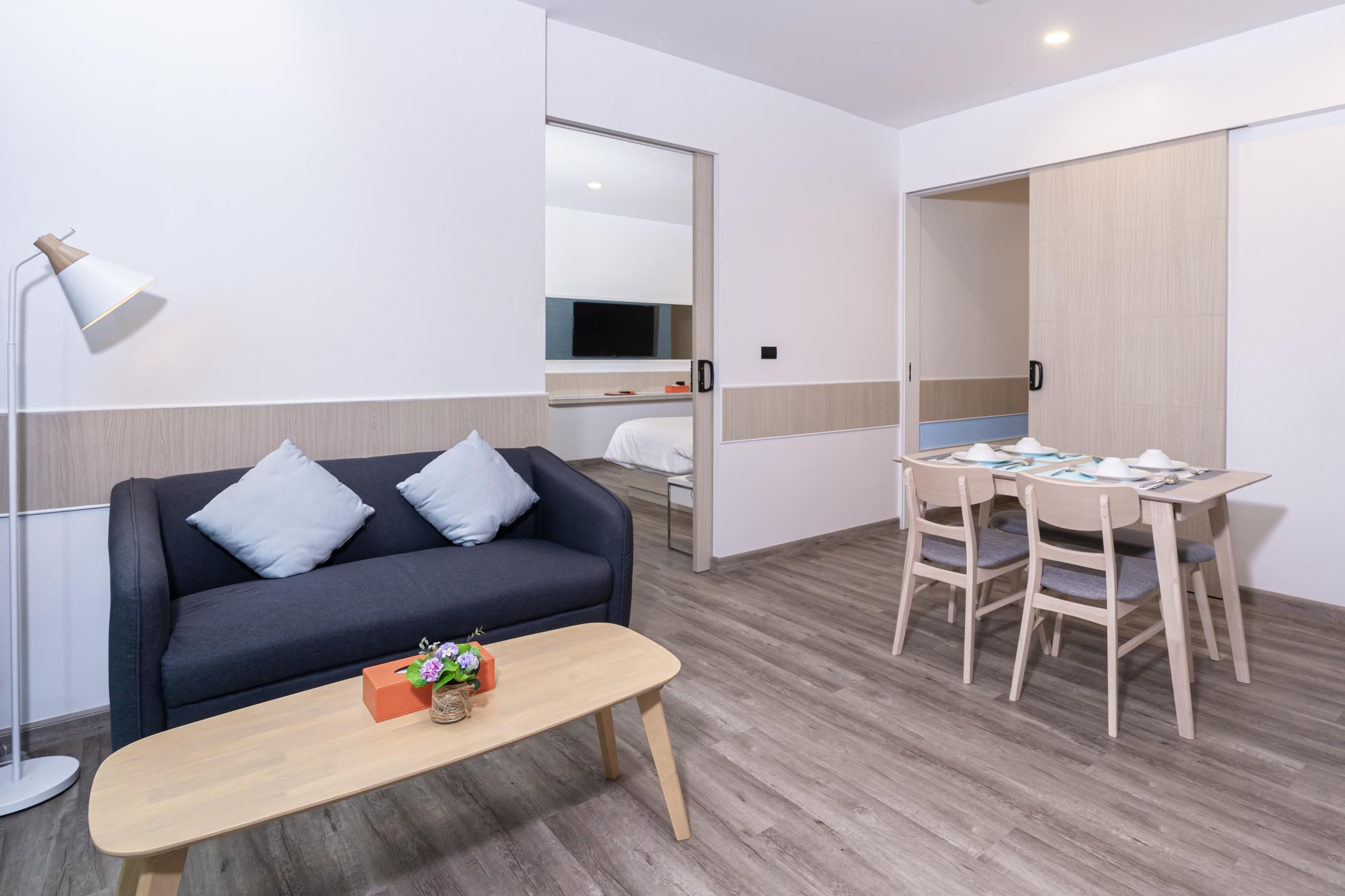 Quarto moderno com sofá, mesinha com um vaso, mesa de jantar com cadeiras e espelho.