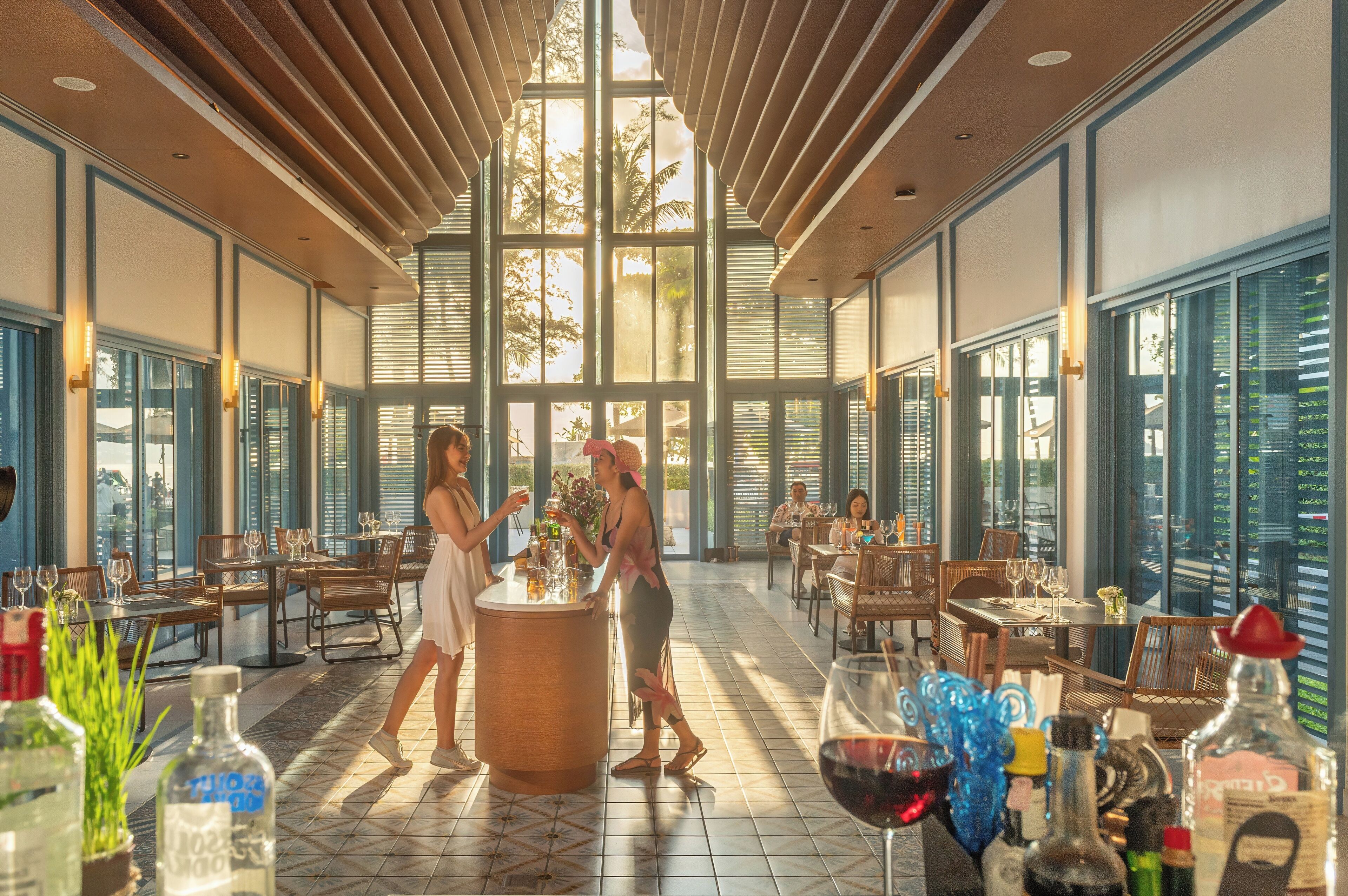 Uma sala de jantar ampla e interna, com pé direito alto, janelas grandes e um bar central.
