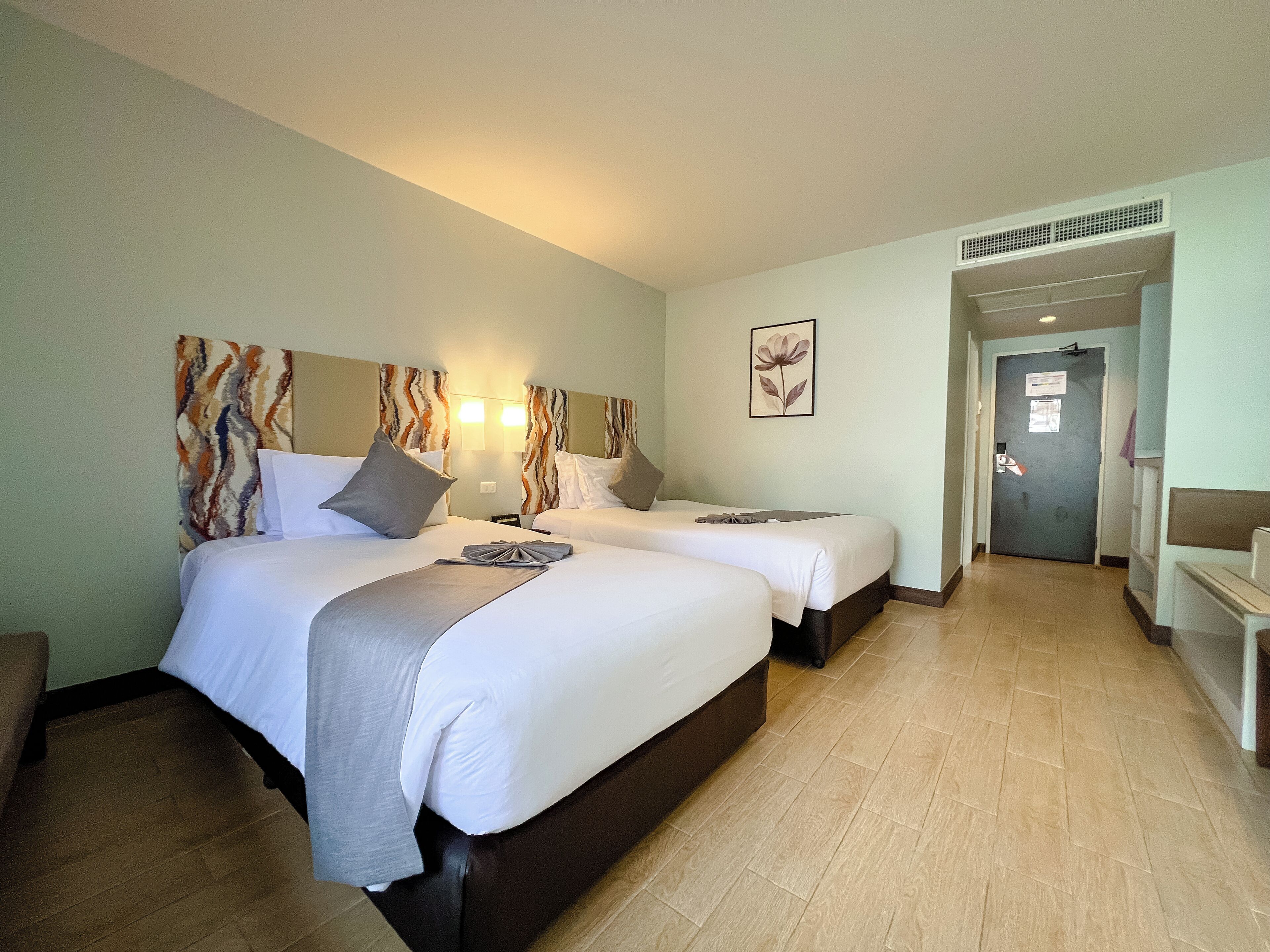 Quarto de hotel com duas camas, uma mesa e uma cadeira. Uma porta dá para um corredor.