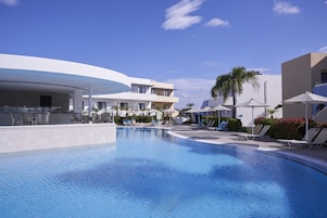 Um resort moderno com piscina, espreguiçadeiras e um céu azul límpido.
