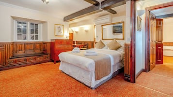 Quarto de hotel com uma cama grande, cómoda de madeira, tapete vermelho e janela com portão de correr branco.