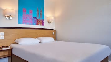 Quarto de hotel com uma cama grande, duas luminárias fixadas na parede e uma pintura da paisagem urbana acima da cama.