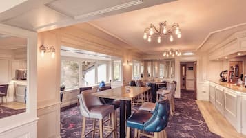Ampla sala de jantar de hotel, com pé direito alto, lustres e bar.
