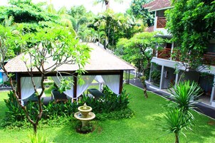 Um jardim com um gazebo, uma fonte e um edifício com varandas.