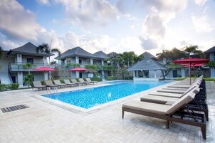 Uma piscina com espreguiçadeiras e guarda-sóis, rodeada por edifícios com varandas e palmeiras.