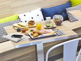 Mesa de café da manhã com croissants, presunto, queijo, torradas, kiwi e um copo de suco de laranja.
