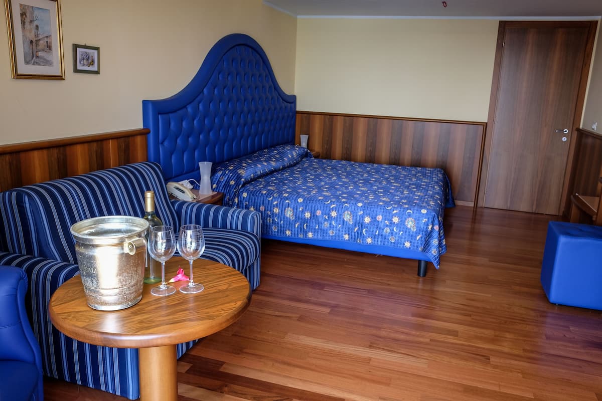 Quarto com uma cama, um sofá, uma pequena mesa com um balde e copos, e chão de madeira.