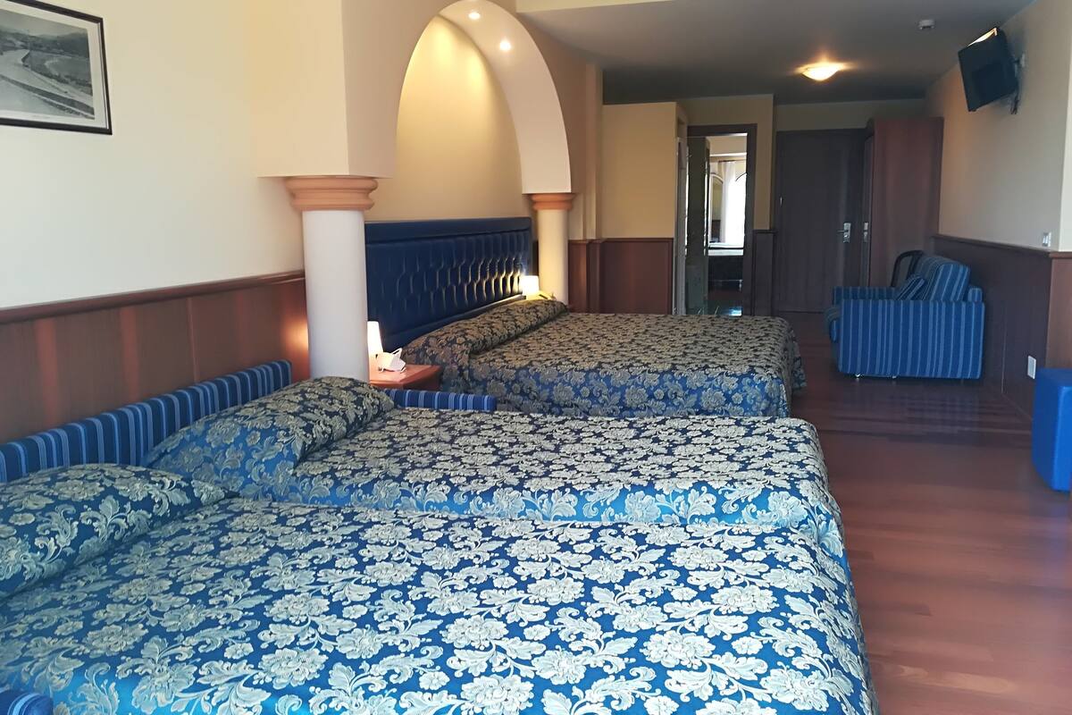 Quarto de hotel com duas camas, um sofá e uma televisão.