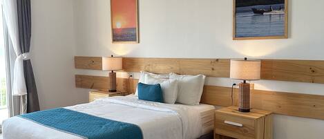 Quarto de hotel moderno com uma cama grande, cabeceira de madeira, duas mesinhas de cabeceira com abajures e duas fotos emolduradas nas paredes.