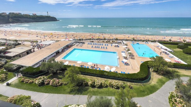 Um resort com uma piscina grande, praia e vista para o oceano.