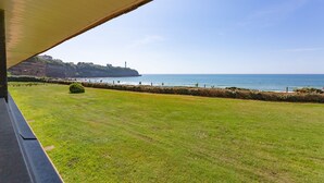 Relvado com um muro de pedra e vista para o mar e um farol.