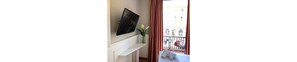 Quarto com televisão de tela plana na parede, mesa de console branca e janela com vista para a cidade.