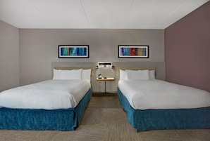Quarto de hotel com duas camas, uma mesinha com telefone e obras de arte nas paredes.