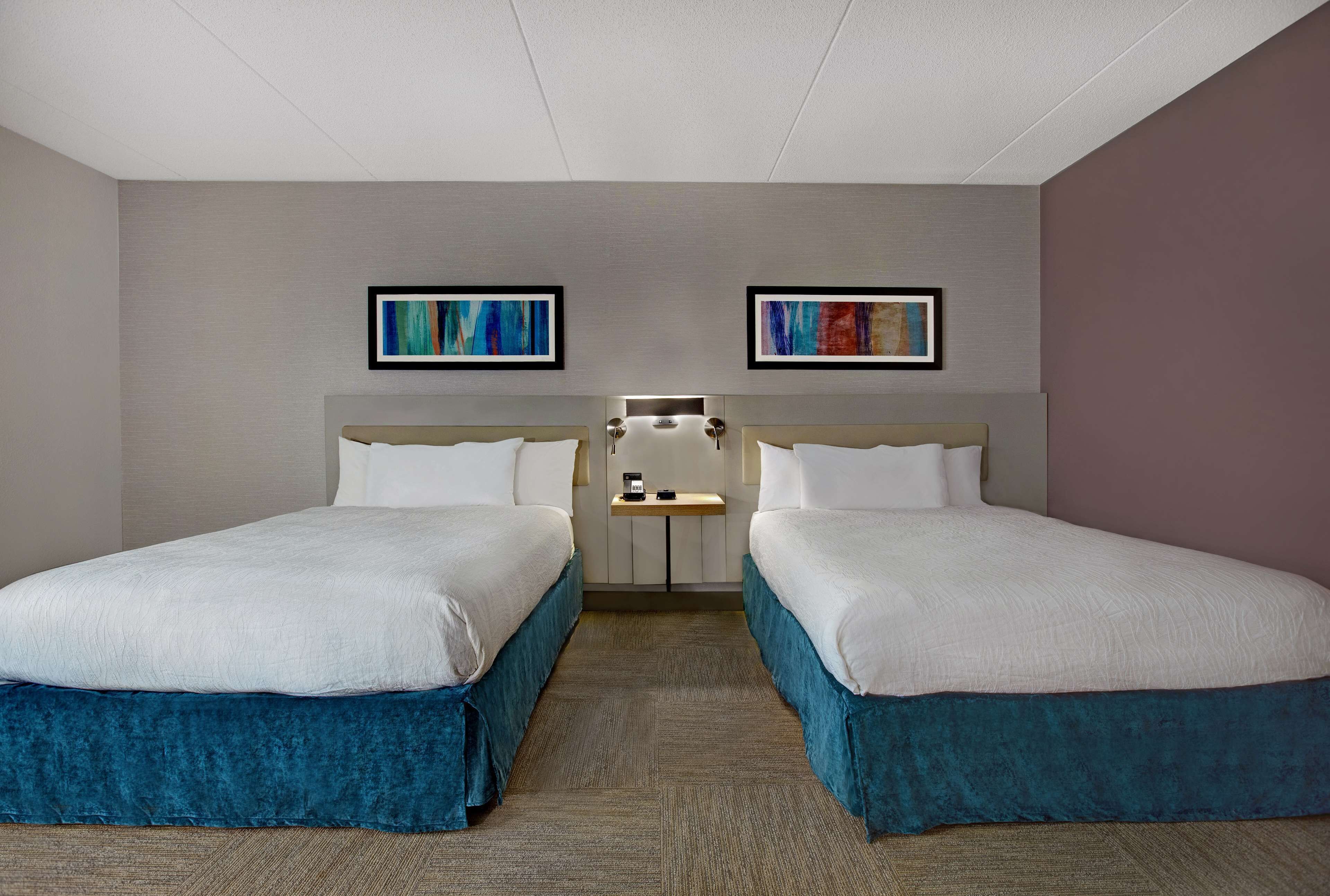 Quarto de hotel com duas camas, uma mesinha e obras de arte nas paredes.