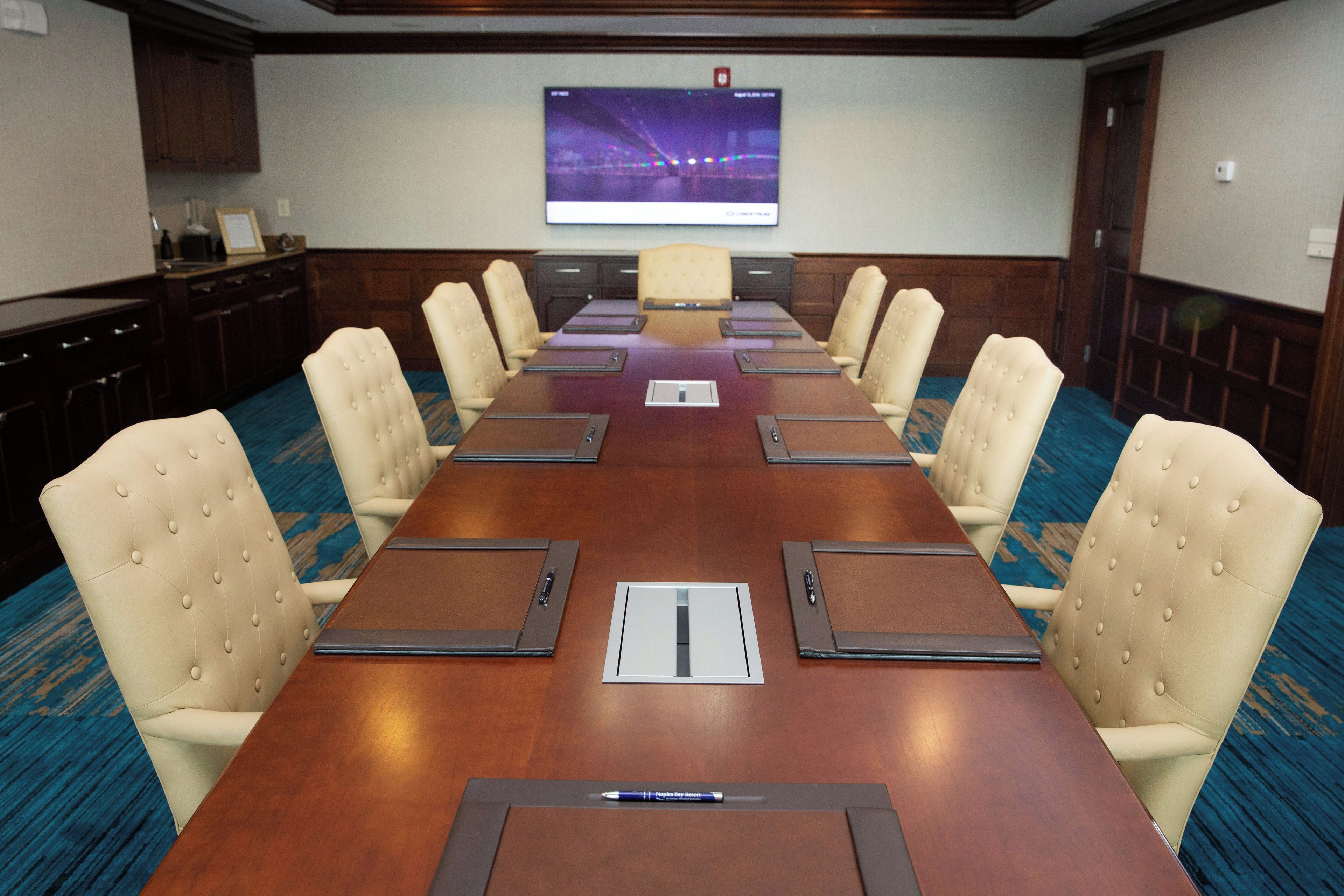 Uma sala de conferências com uma mesa comprida, várias cadeiras, uma tela de projetor e piso coberto de carpete.