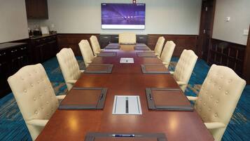 Uma sala de conferências com uma mesa comprida, várias cadeiras, uma tela de projetor e piso coberto de carpete.