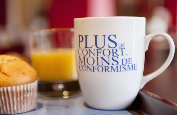 Uma caneca branca com texto, um muffin e um copo de sumo de laranja sobre um prato.