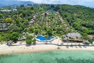 Vista aérea de um resort com uma piscina central, vilas na praia e vegetação exuberante.