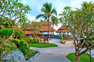 Um resort com construções de telhado de palha, um caminho pavimentado e vegetação exuberante.