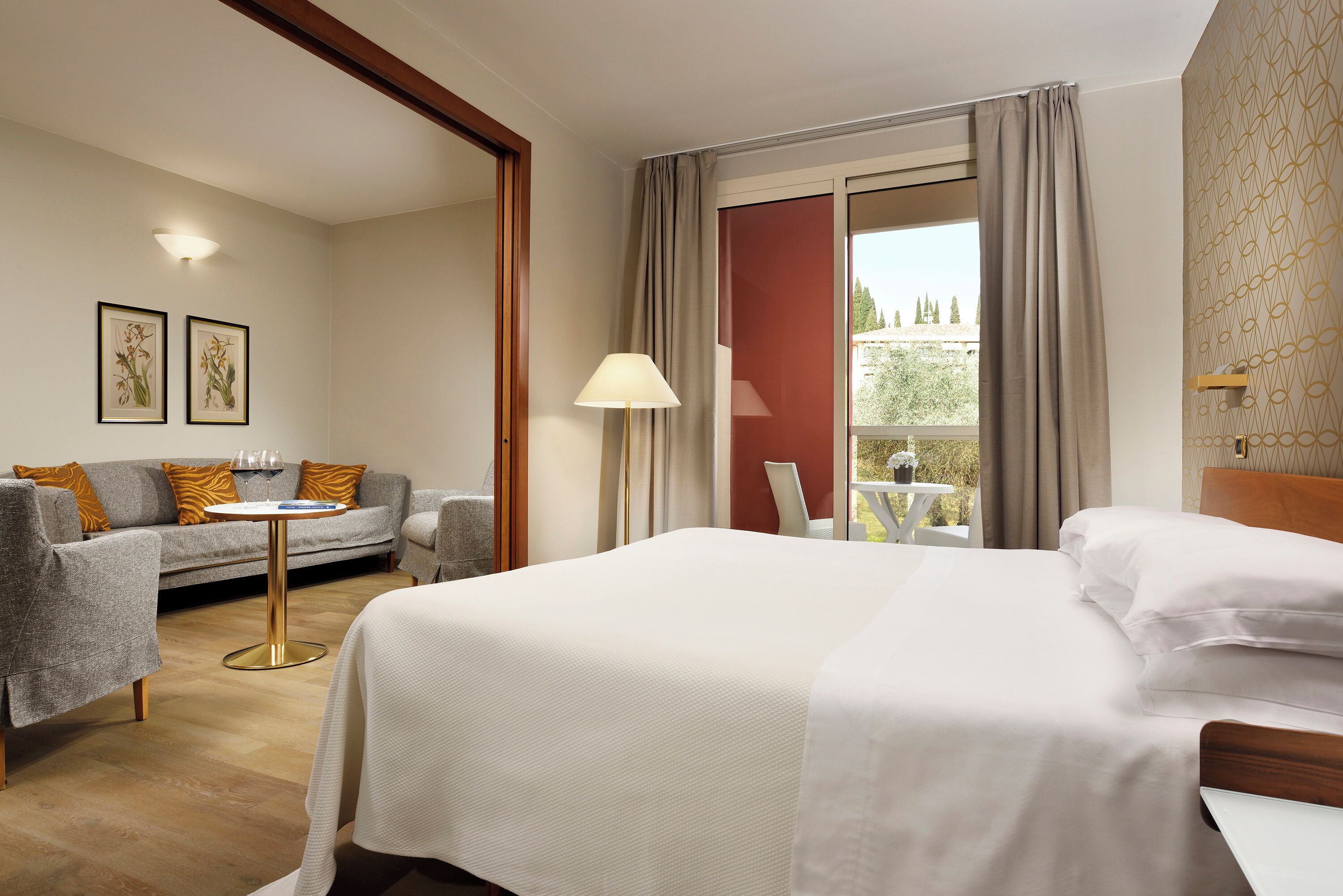 Quarto de hotel com cama, sofá, uma mesa pequena e janela com cortinas.