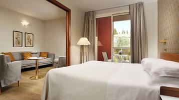 Quarto de hotel com cama, sofá, uma mesa pequena e janela com cortinas.