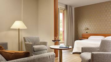 Quarto de hotel com uma cama, duas poltronas, uma mesinha e um abajur.