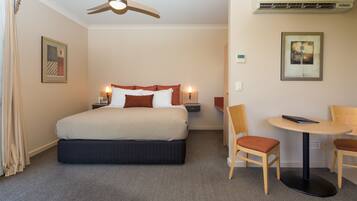 Quarto de hotel com cama, escrivaninha com cadeira, ventilador de teto e aparelho de ar condicionado.