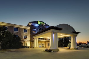 Um hotel Holiday Inn Express & Suites com entrada coberta e um amplo estacionamento.